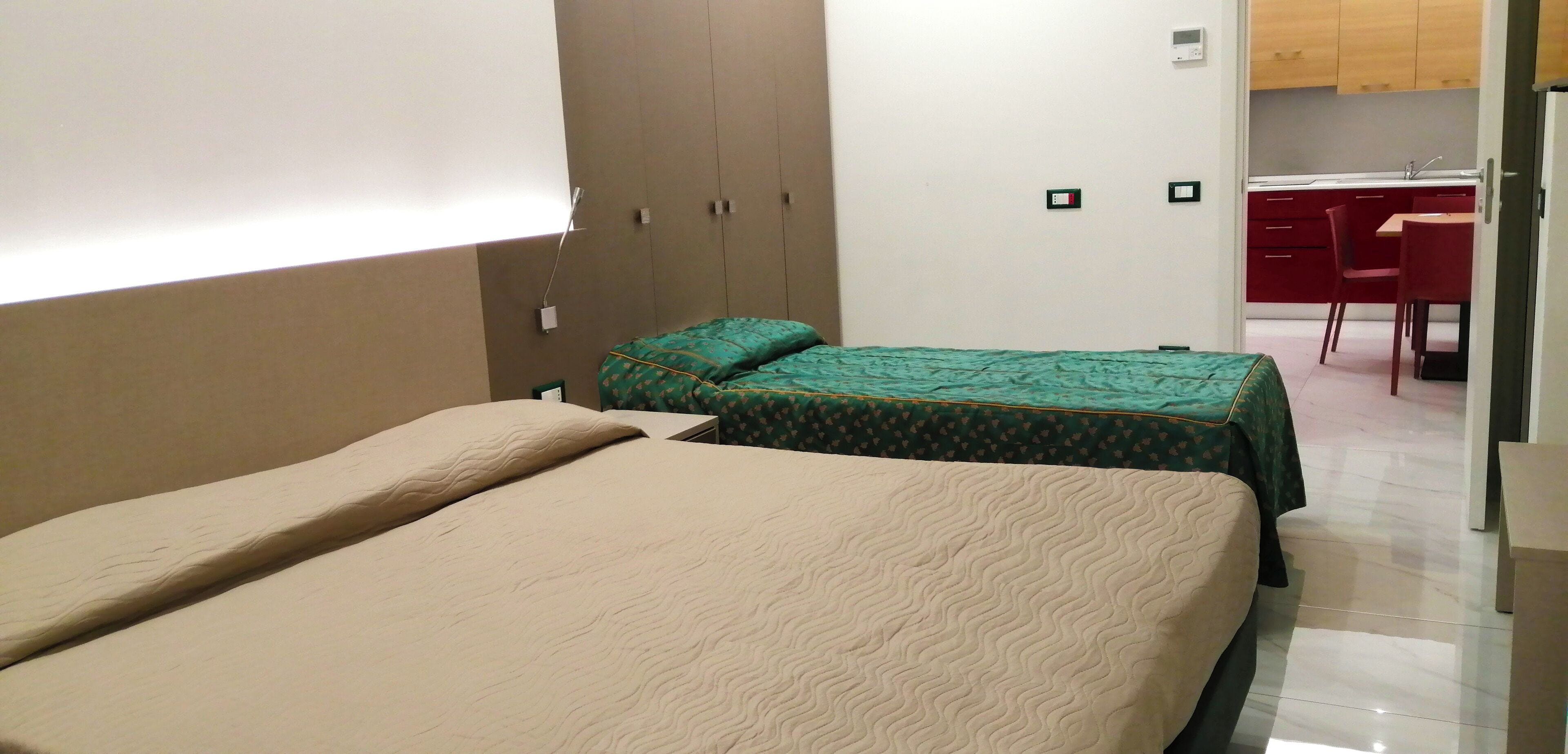 Quarto com duas camas, um kitchenette e uma cadeira vermelha.