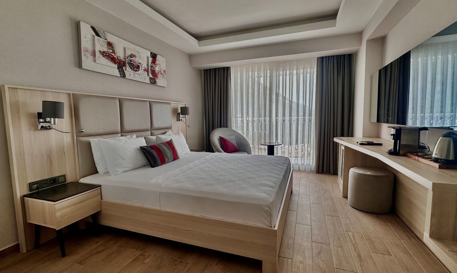 Quarto de hotel moderno com uma cama grande, uma mesa com cafeteira, uma cadeira e uma TV.
