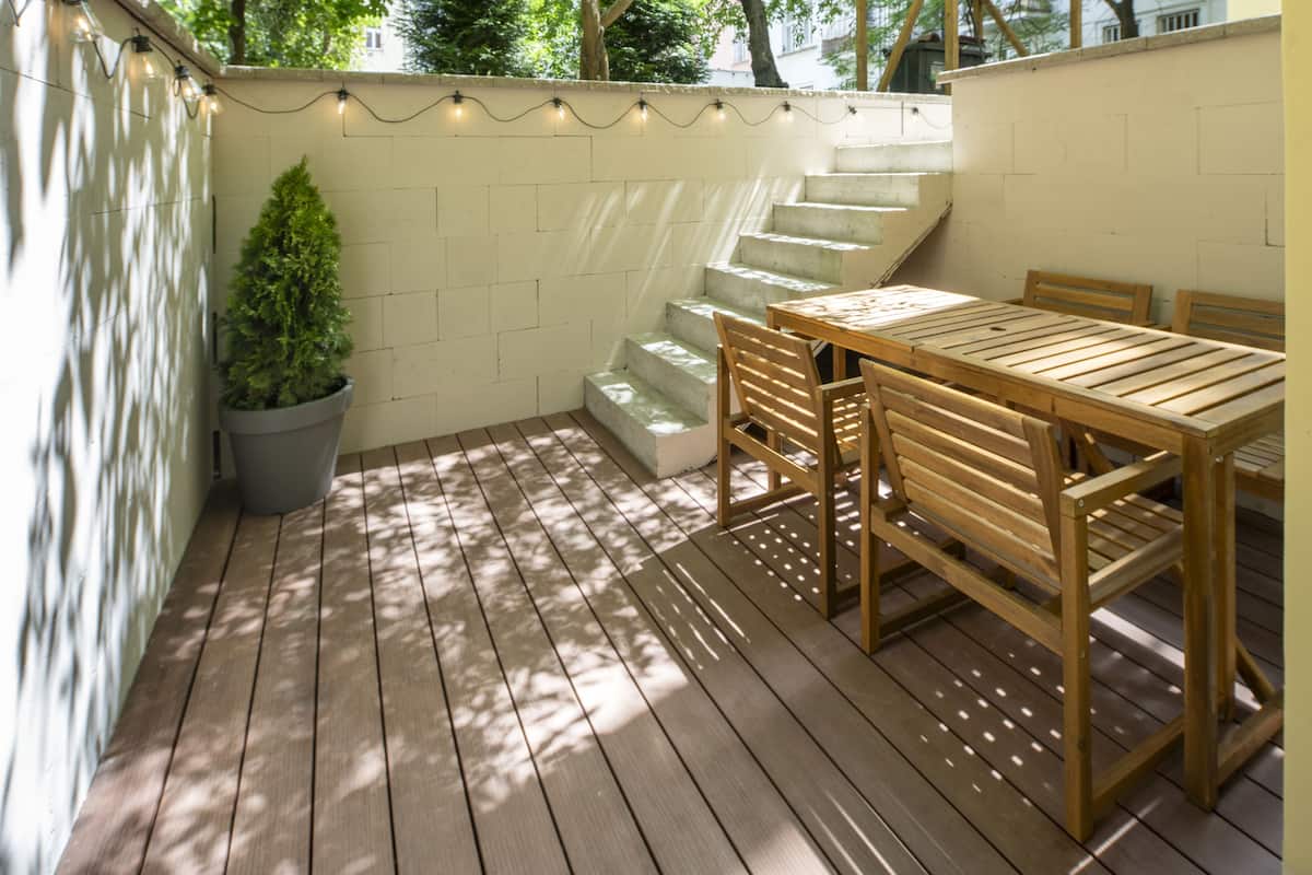 Um deck de madeira com mesa, cadeiras, um vaso de planta e uma escadaria.