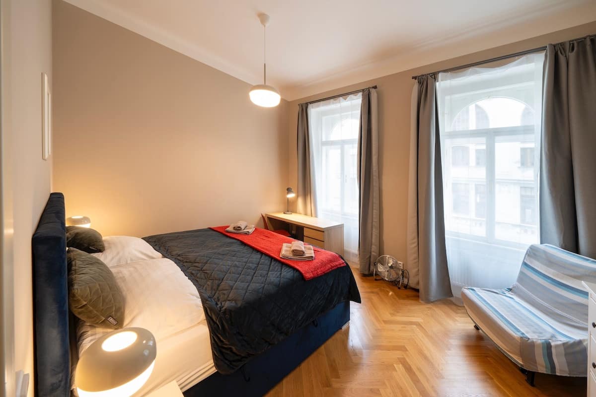 Quarto com cama, mesa de cabeceira, escrivaninha e sofá.