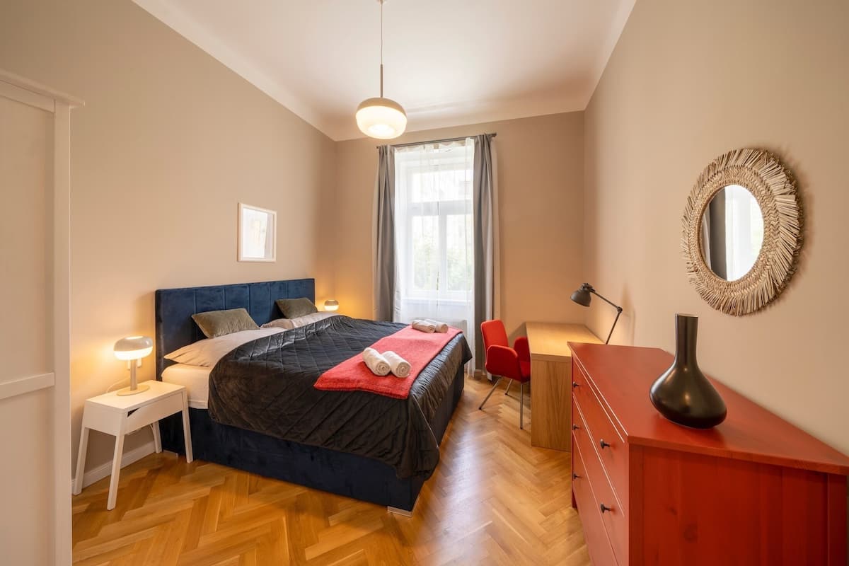 Quarto com cama, mesas de cabeceira, escrivaninha, cadeira, cômoda, espelho e janela.