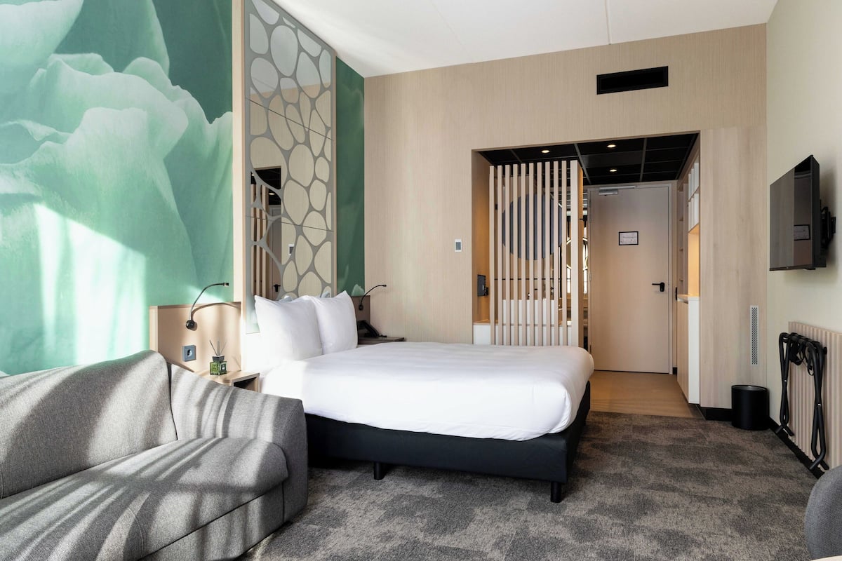 Quarto de hotel com cama, sofá, televisão e parede com design geométrico.