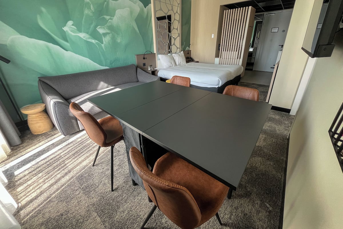 Quarto de hotel com cama, sofá, mesa de jantar com cadeiras e um grande mural floral na parede.