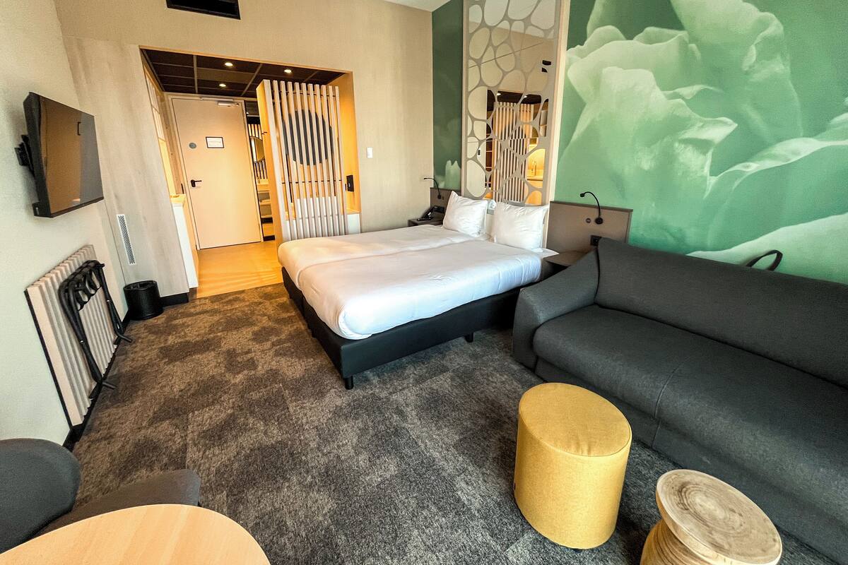 Quarto de hotel com cama, sofá, uma pequena mesa e parede com um desenho abstrato em verde.