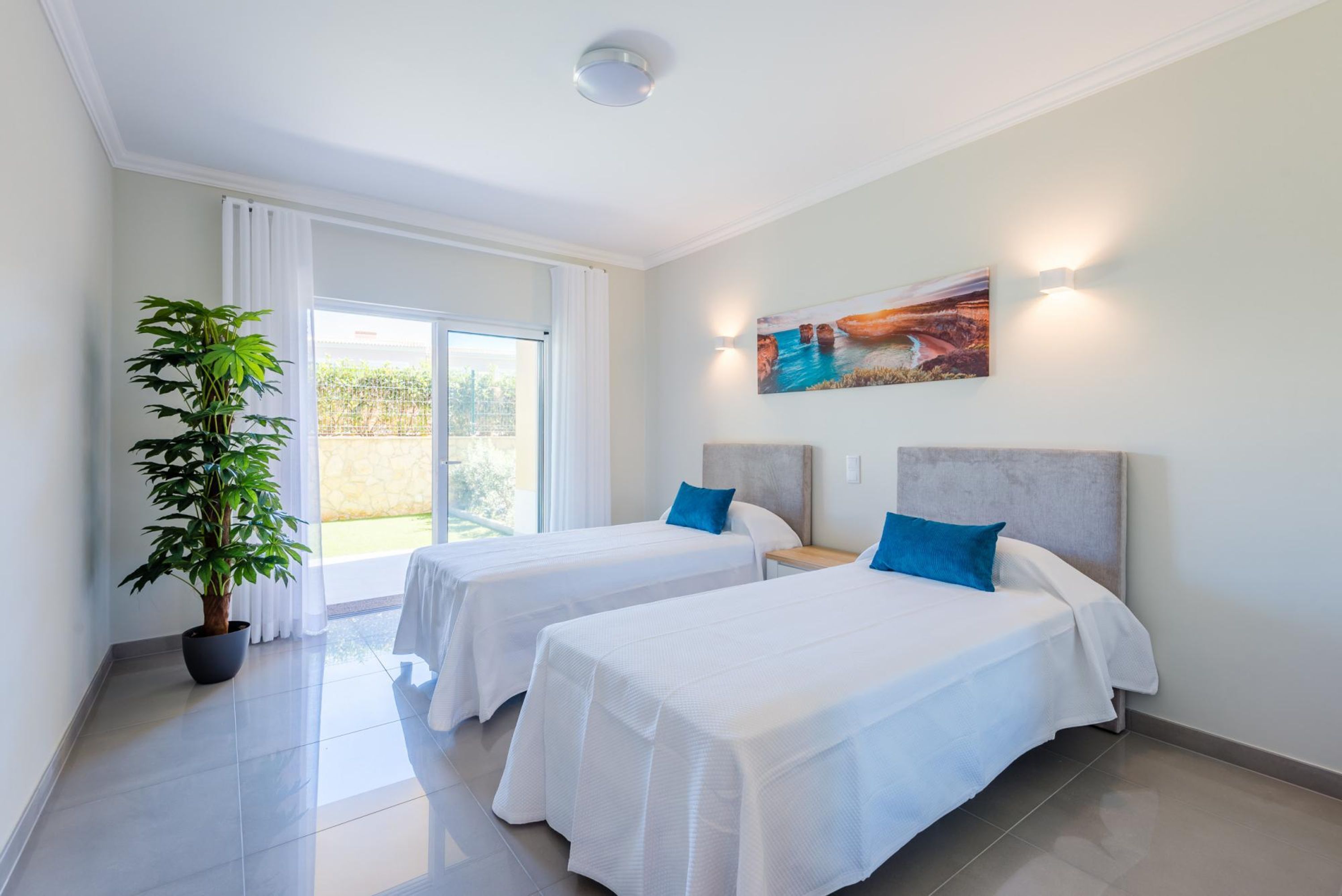 Quarto de hotel com duas camas, um vaso de planta, um quadro e vista através de uma porta de correr.