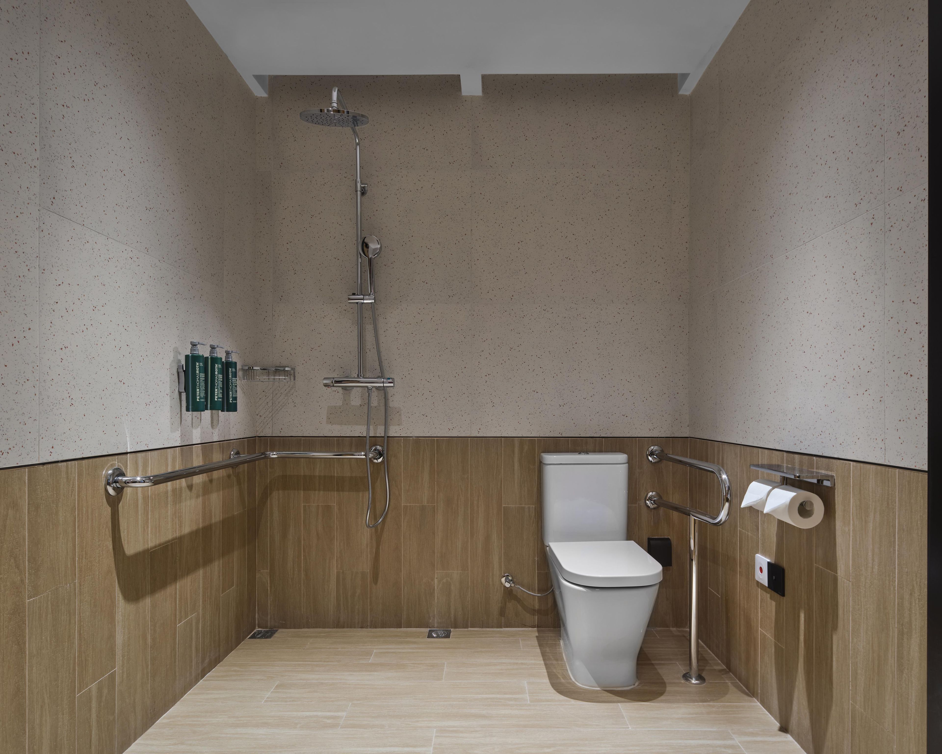 Uma casa de banho moderna com chuveiro, sanita e barras de apoio.