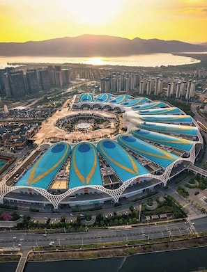 Um estádio grande com várias seções de cobertura azul e amarela, rodeado por edifícios altos e uma massa de água.
