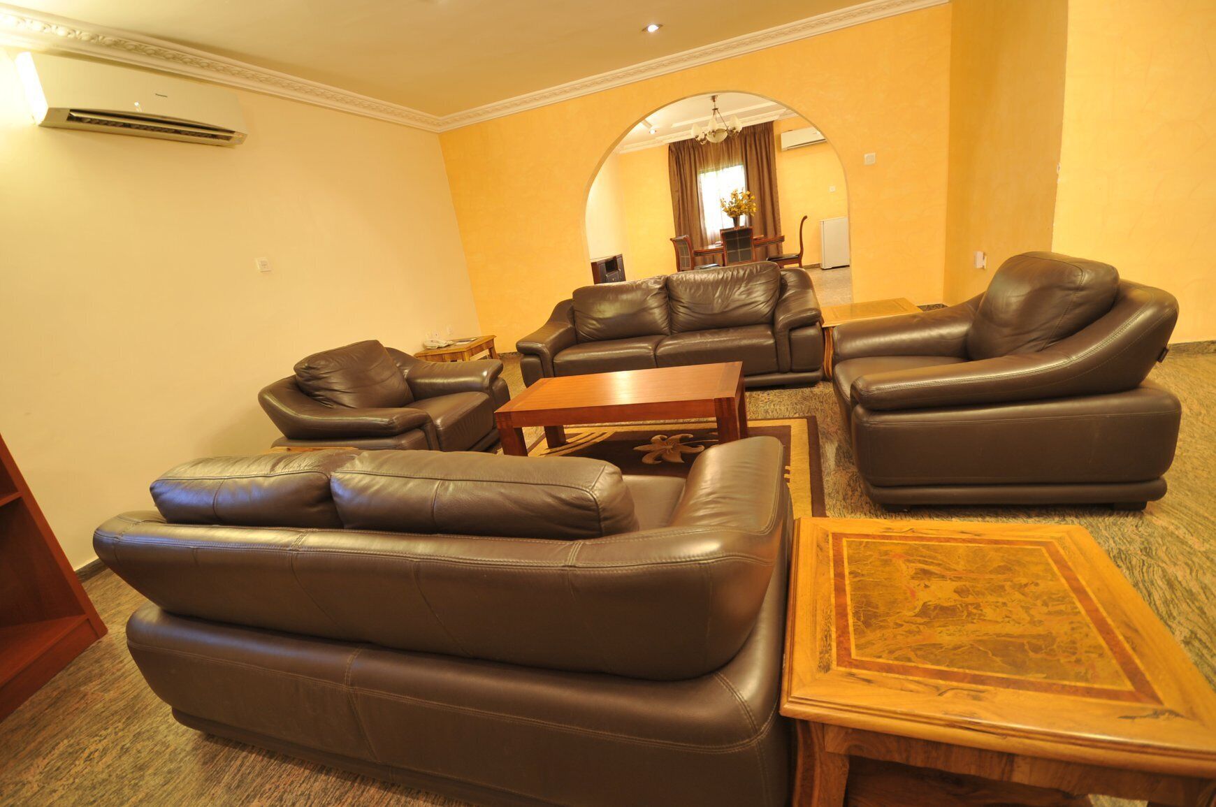 Uma sala de estar com sofás de couro, uma mesa de centro de madeira e piso coberto de carpete.