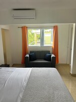 Quarto de hotel com cama, sofá com almofadas, janela com cortinas e ar condicionado.
