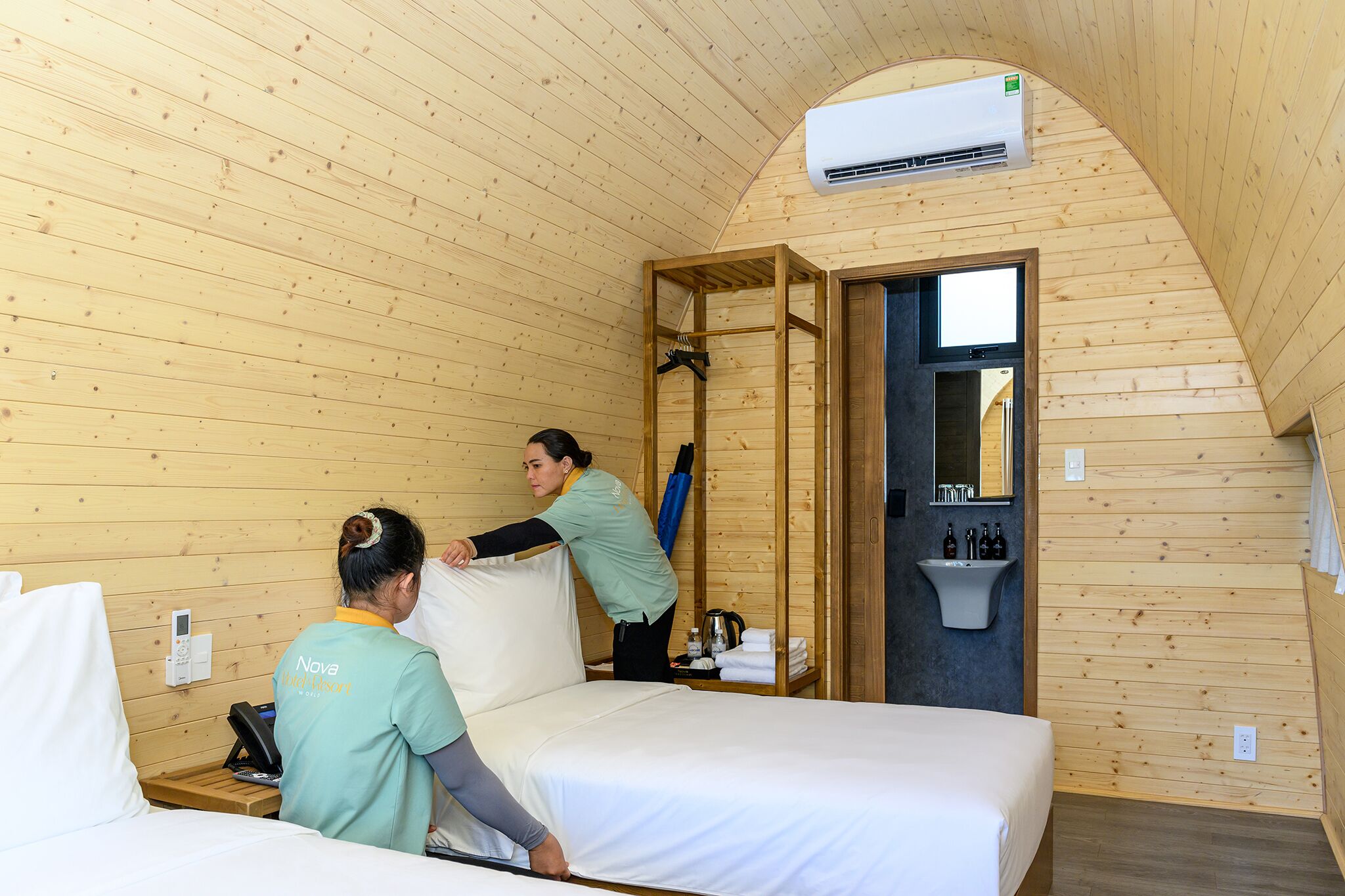 Quarto de cabana de madeira com duas camas, um guarda-roupa de madeira, uma pia e um aparelho de ar condicionado.