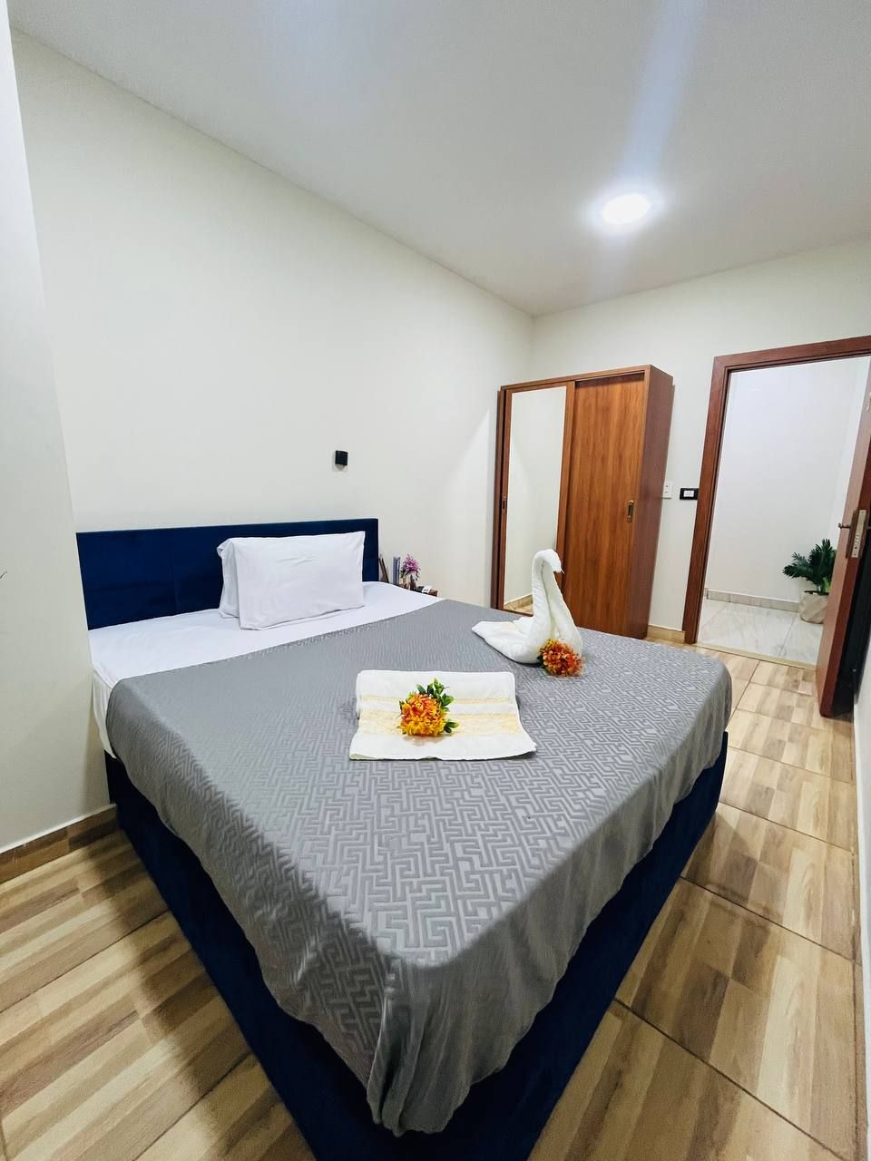 Cama arrumada com cabeceira azul, travesseiro em formato de cisne e toalha decorativa com flores.