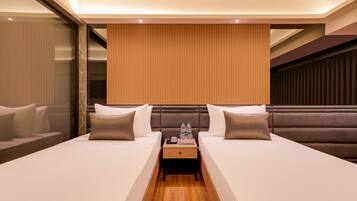 Quarto de hotel moderno com duas camas, uma cabeceira de madeira e uma mesa de cabeceira com telefone e garrafas de água.