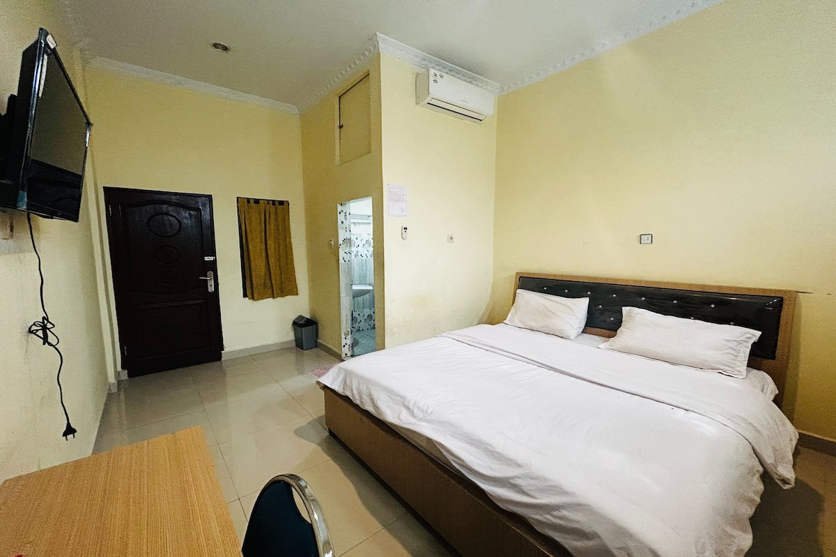 Quarto de hotel com cama, televisão fixada na parede, porta e unidade de ar condicionado.