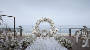 Decoração de casamento com arco de flores e corredor em deck de madeira com vista para o mar.