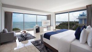 Quarto de hotel moderno com uma cama grande, área de estar, televisão e vista para o oceano.