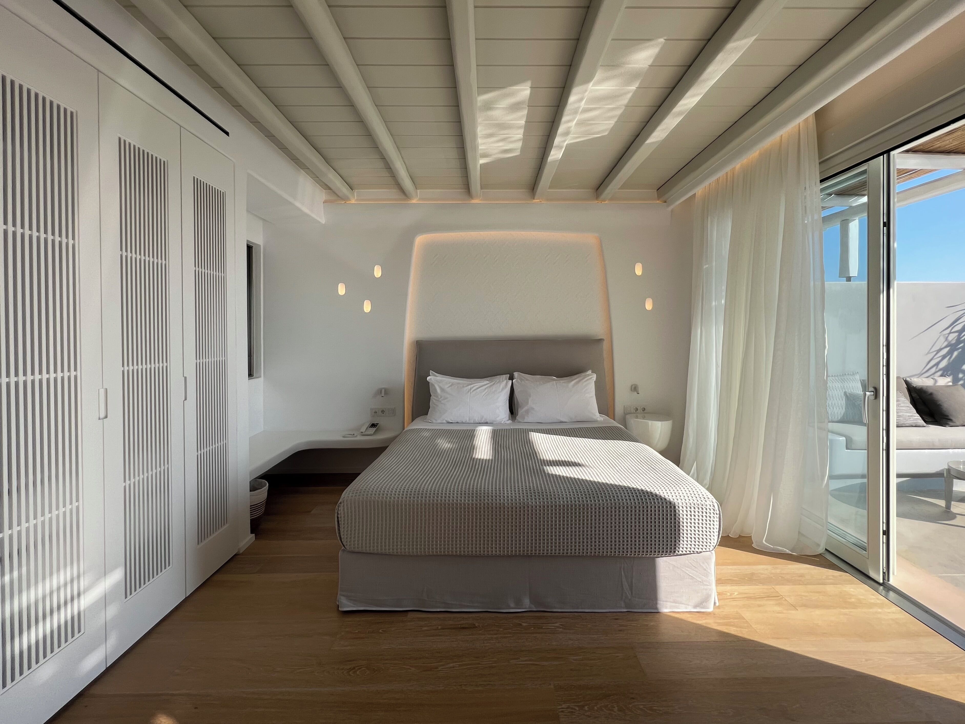 Quarto moderno com uma cama grande, mesa de cabeceira e vista para o exterior por uma porta de correr.