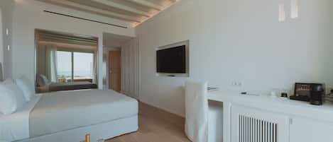 Quarto de hotel moderno com cama, escrivaninha, televisão e vista para a praia.