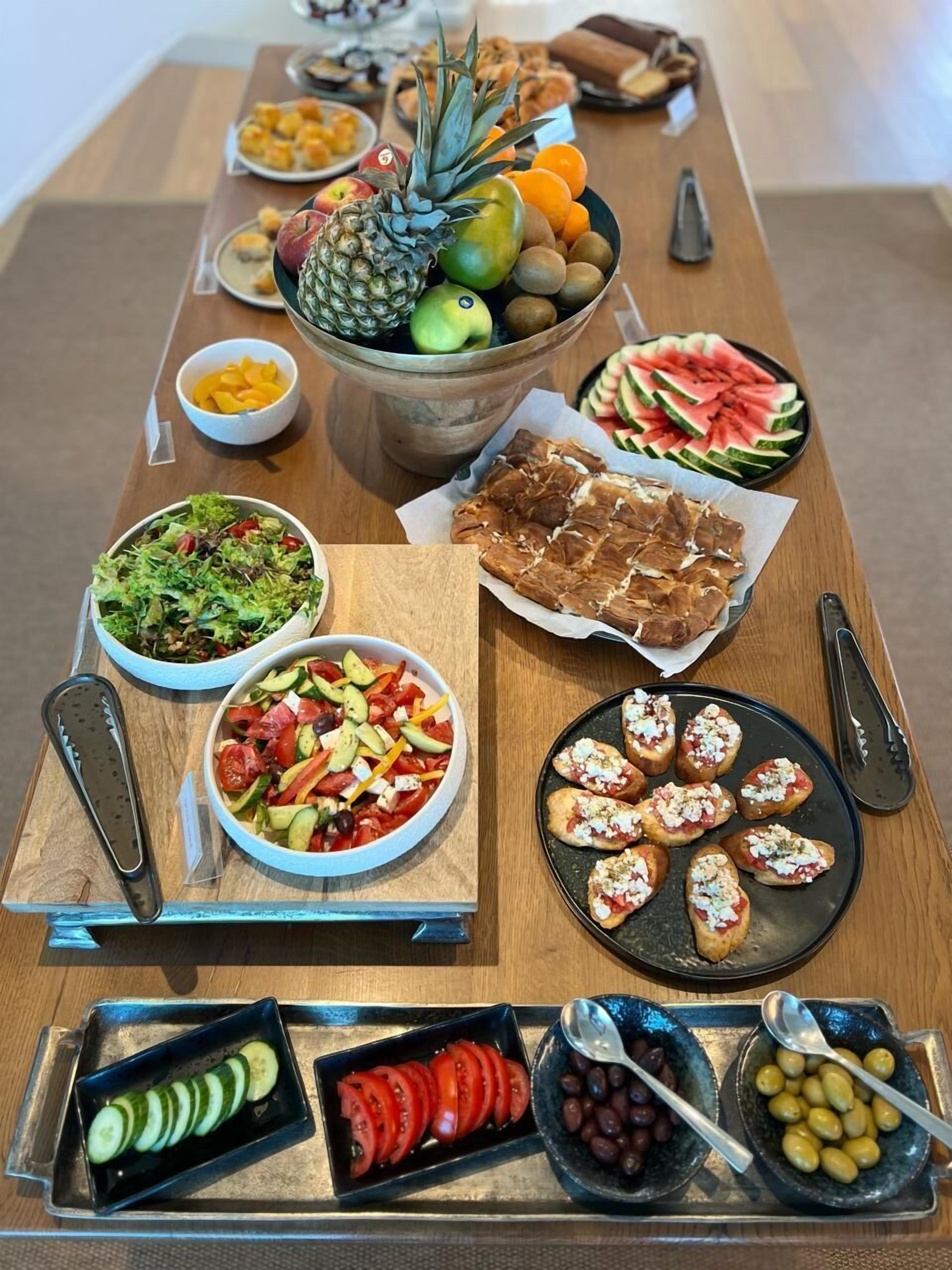 Uma mesa com diversos alimentos, incluindo frutas, saladas e aperitivos.