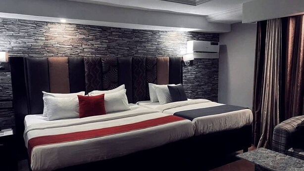 Quarto de hotel moderno com uma cama grande, parede de destaque em pedra e área de estar com sofá.