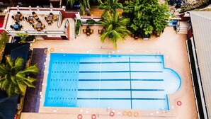 Vista aérea de uma piscina com várias pistas de natação, rodeada por áreas de estar ao ar livre e palmeiras.