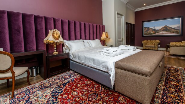 Quarto com uma cama grande, mesa de cabeceira, cadeira, banco e uma janela ampla.