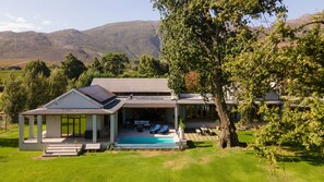 Uma casa moderna com piscina, varanda coberta e vista para montanhas.