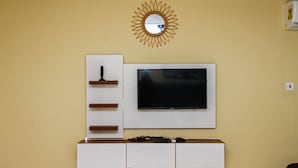 Uma TV fixada na parede com um módulo de entretenimento branco embaixo, apresentando um espelho acima e uma pequena prateleira com um controle remoto.