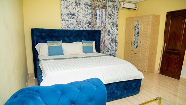 Quarto com uma cama grande, uma poltrona azul estofada e um guarda-roupa.