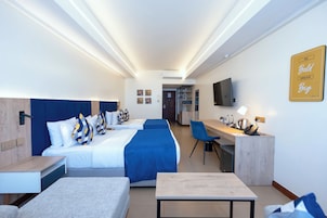 Quarto de hotel com duas camas, uma escrivaninha, uma cadeira e uma televisão.