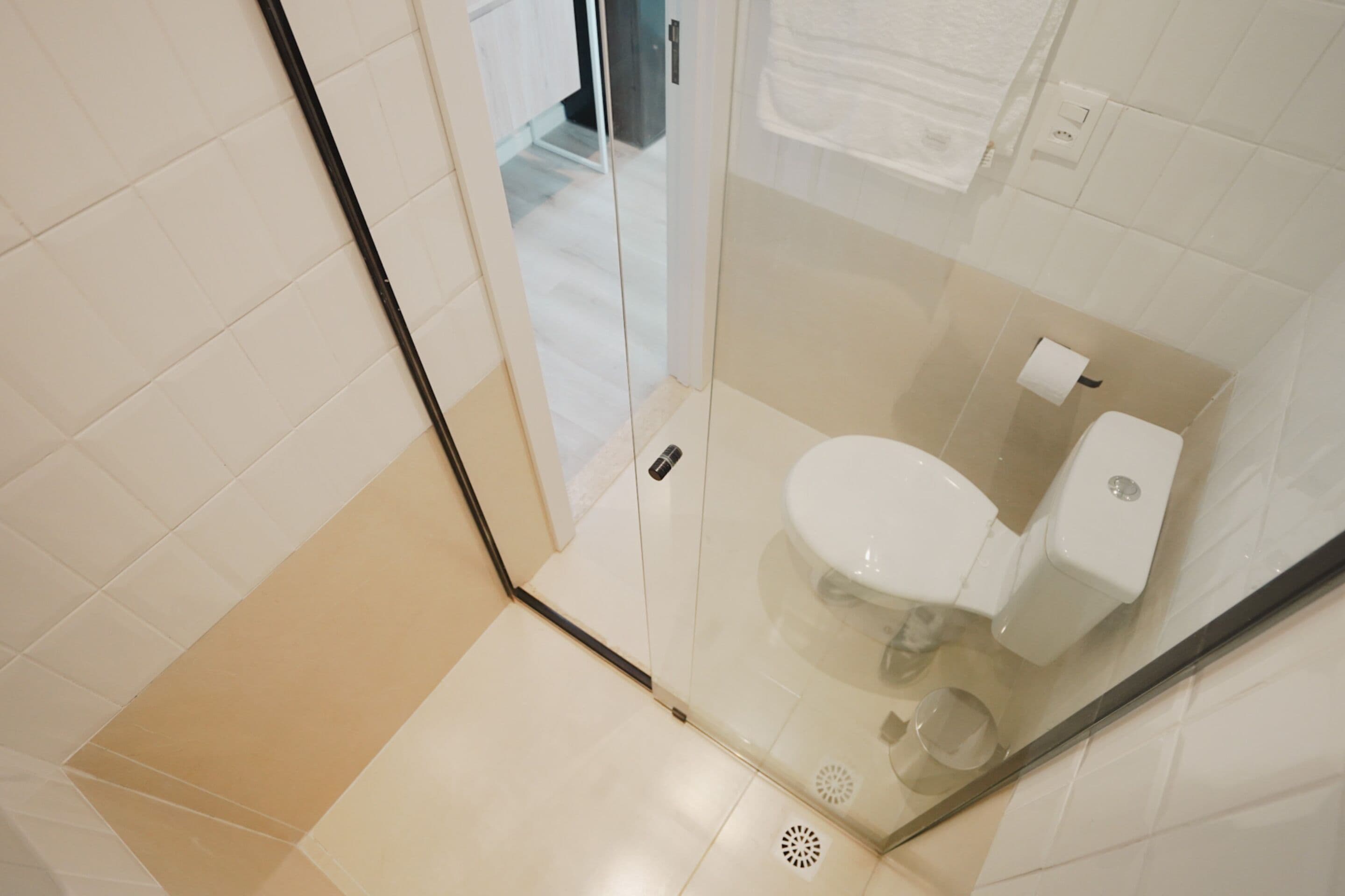 Um banheiro moderno com box de vidro, vaso sanitário branco e porta-toalhas visível.