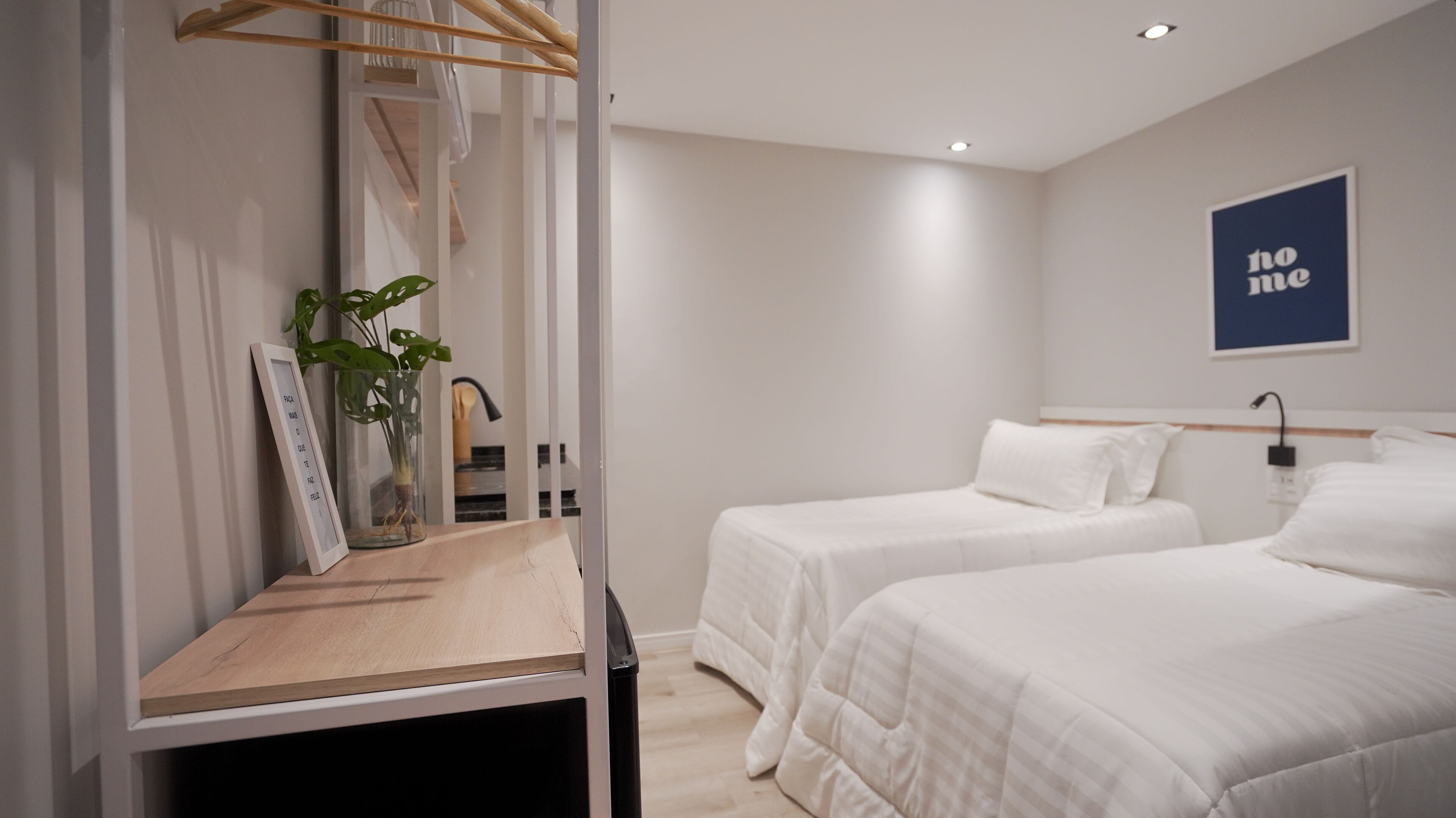 Quarto de hotel com duas camas de solteiro, um banco de madeira, uma planta em vaso e um quadro na bancada.