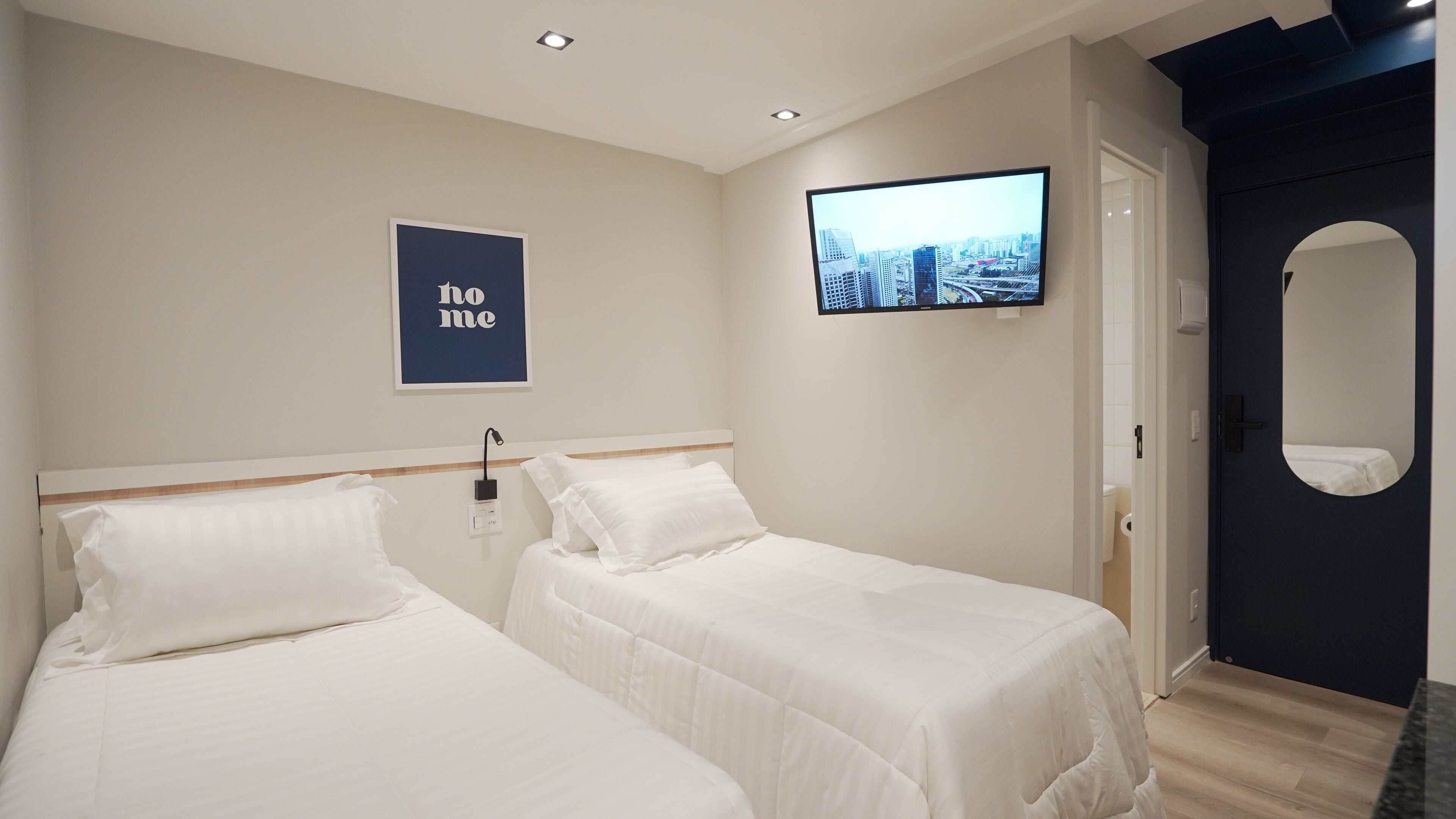 Quarto de hotel com duas camas, televisão na parede, um cartaz com a expressão 'não me perturbe' e um espelho no canto.