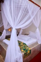 Cama com roupa de cama branca e dossel, manta estampada e mesa de cabeceira com abajur.