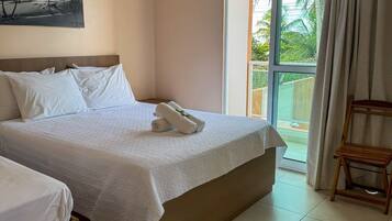 Quarto de hotel com uma cama grande, uma mesa pequena, uma cadeira e uma varanda com cortinas.