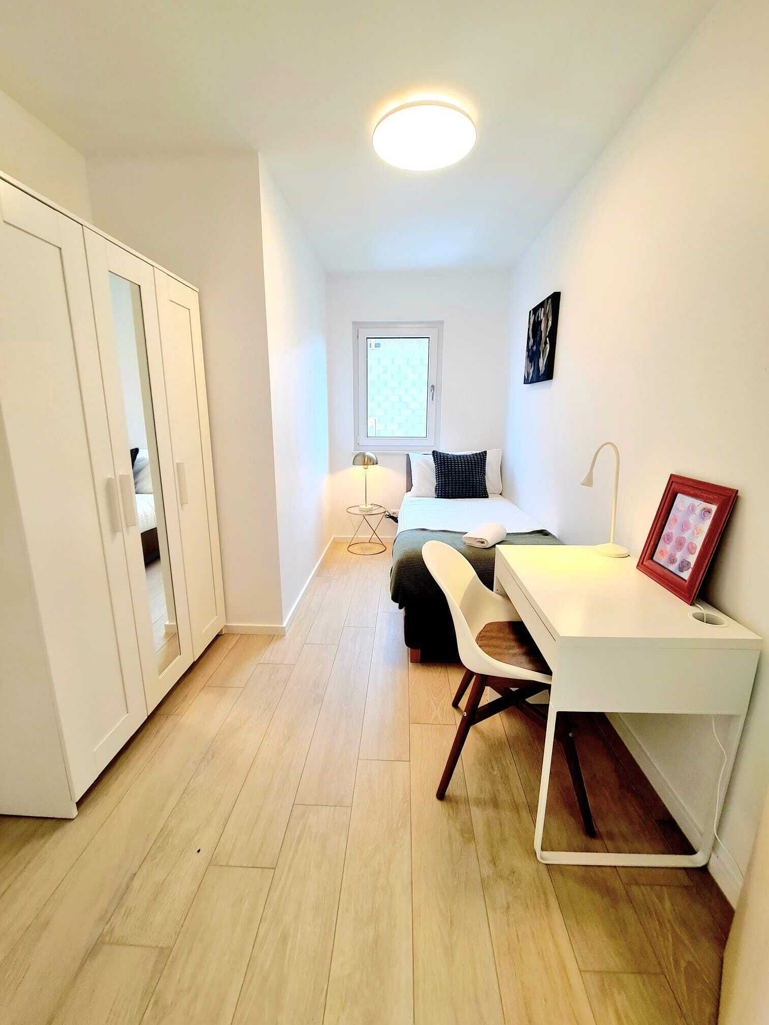 Quarto compacto com cama, escrivaninha, cadeira, armário e janela.