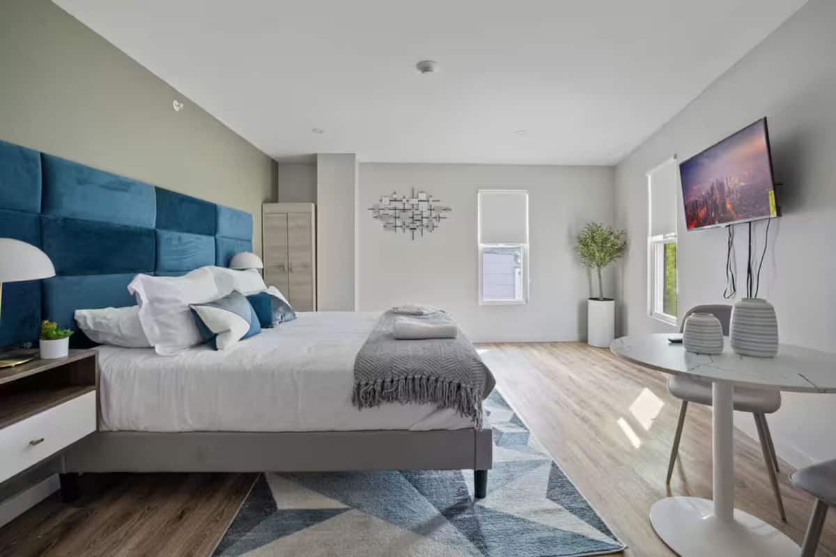 Quarto moderno com uma cama grande, mesas de cabeceira, uma escrivaninha e uma televisão.