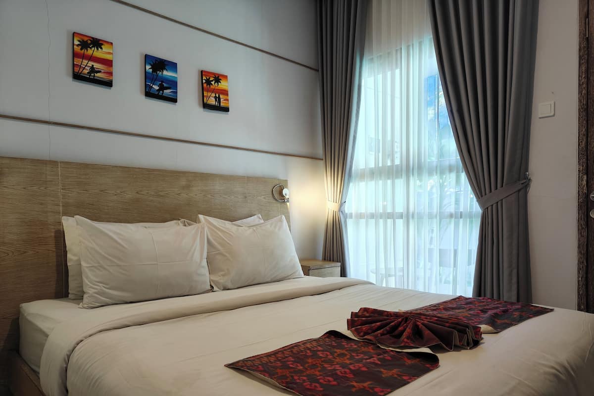 Quarto de hotel com uma cama grande, cabeceira de madeira e três obras de arte nas paredes retratando cenas tropicais.