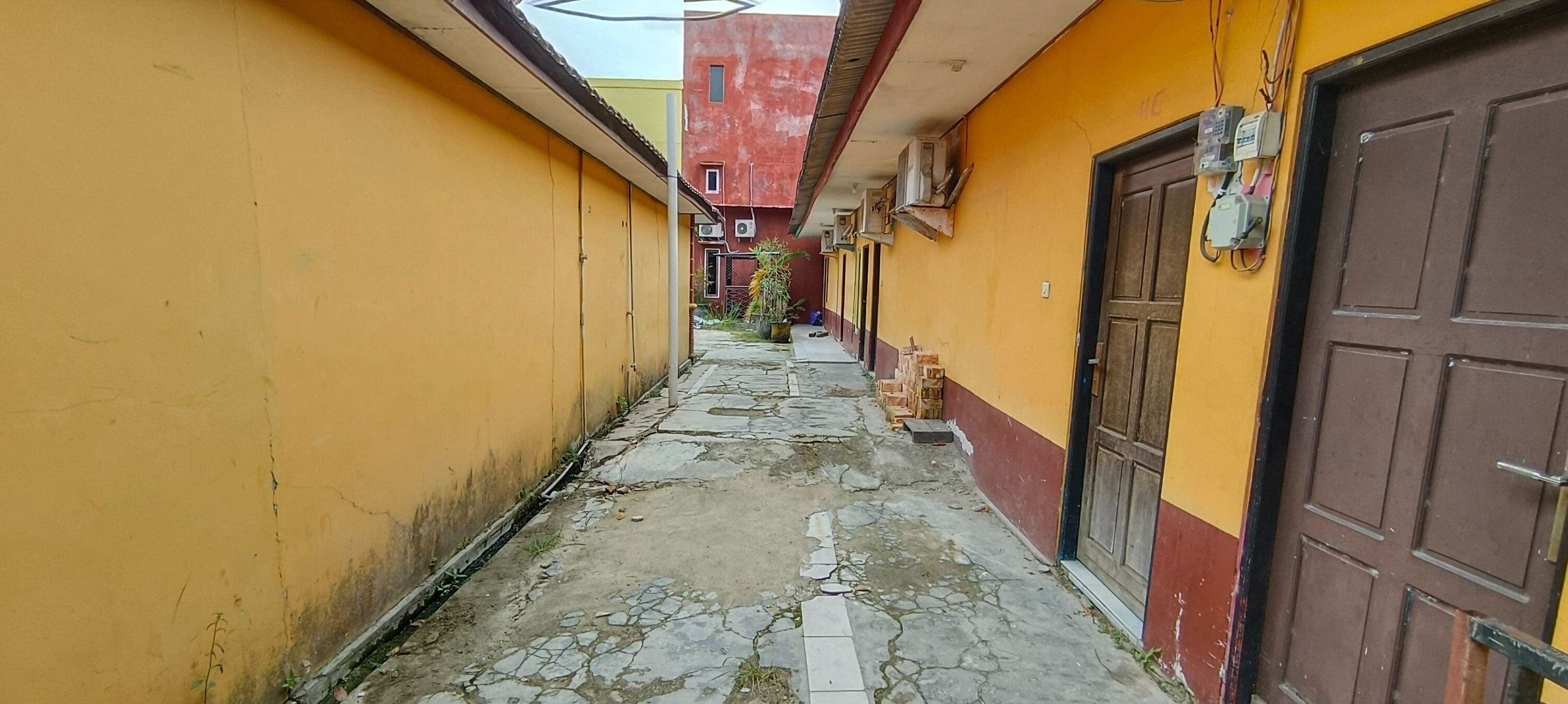Uma passagem estreita com uma parede amarela de um lado e um edifício vermelho do outro.
