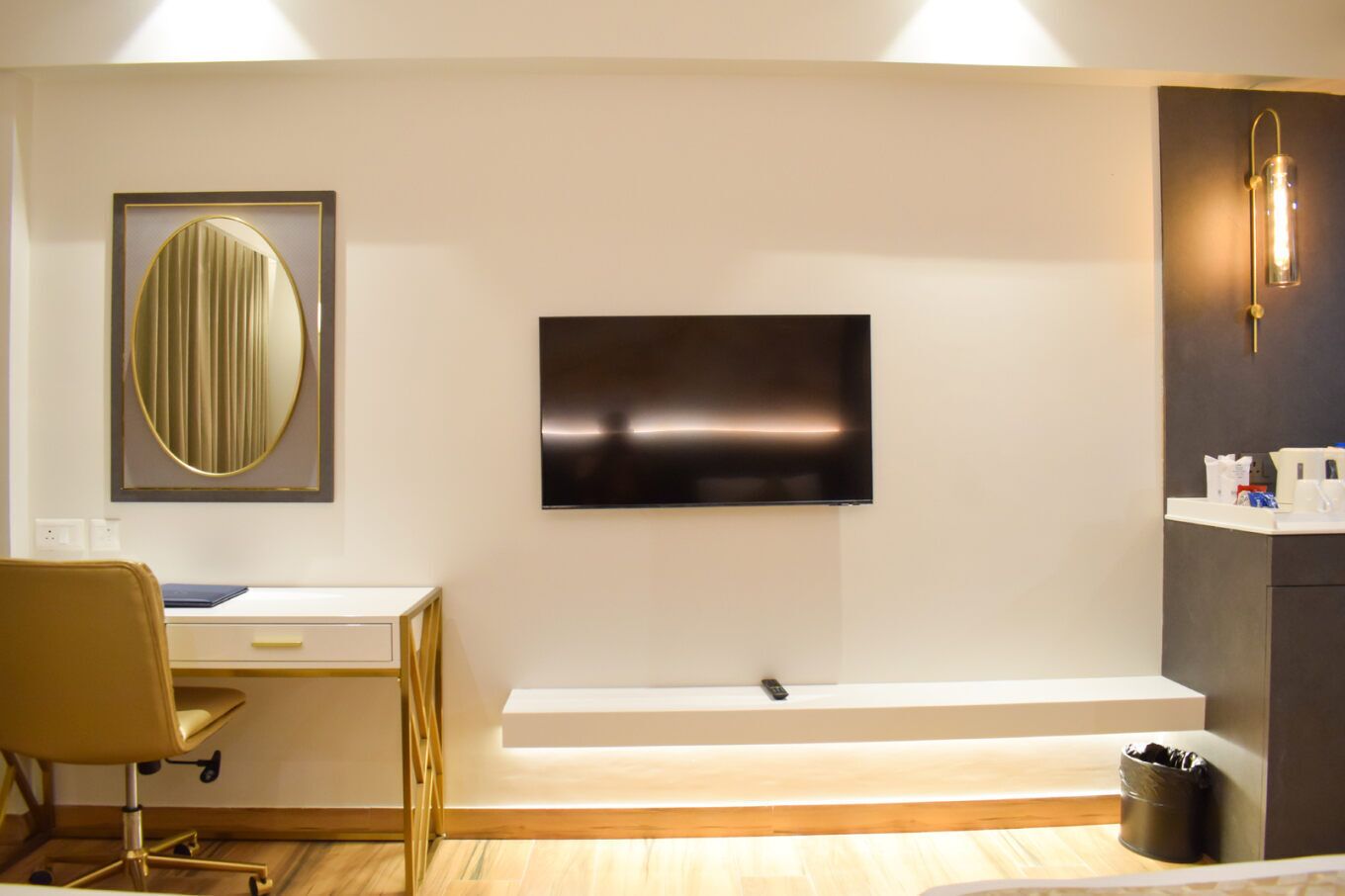 Quarto de hotel moderno com televisão de tela plana na parede, uma mesa com cadeira e um pequeno banco.
