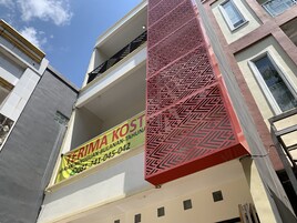 Fachada de prédio com um padrão geométrico vermelho chamativo e uma placa amarela anunciando venda de imóvel.