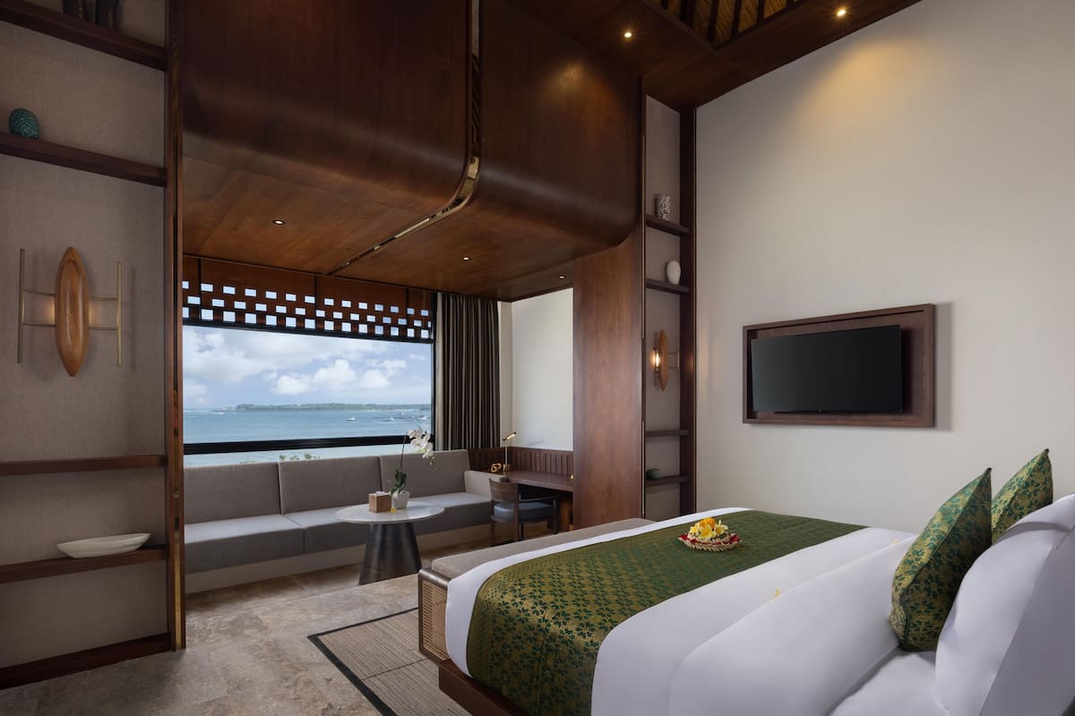 Quarto de hotel moderno com uma cama grande, área de estar vista e varanda com vista para o mar.