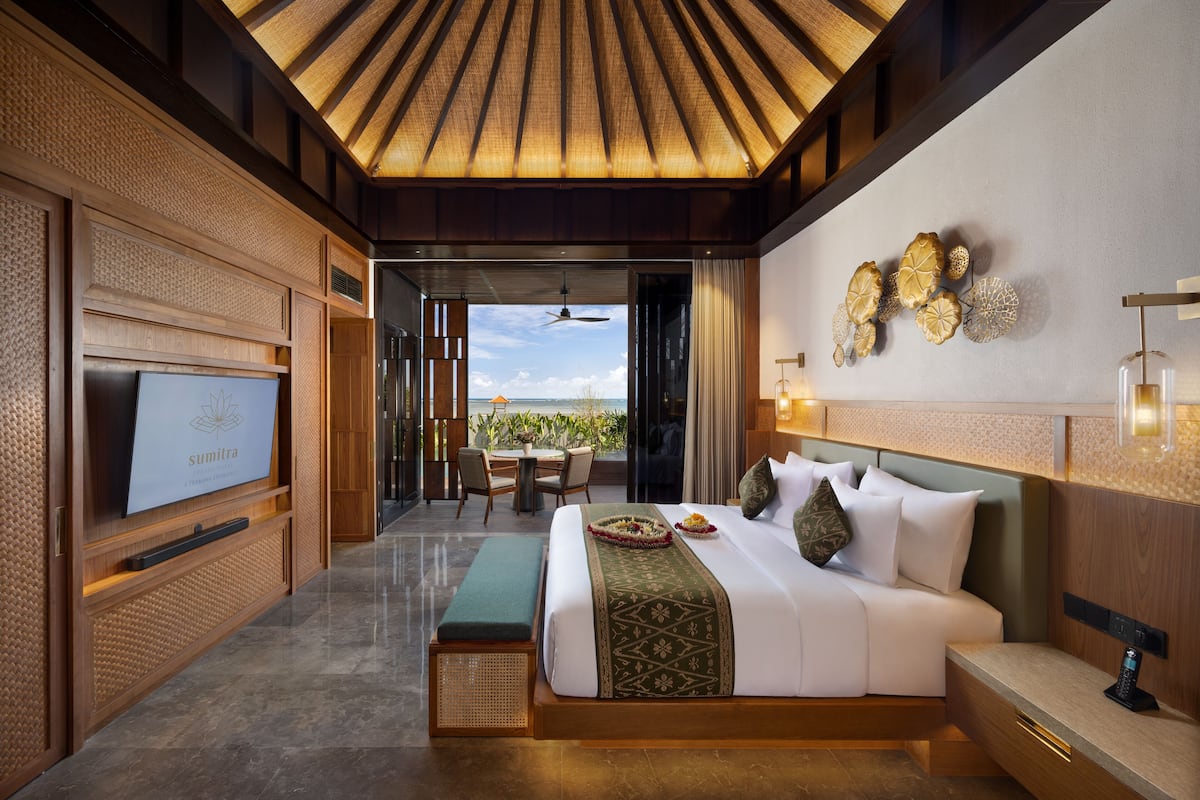 Quarto de hotel moderno com uma cama grande, televisão, área de refeições e vista para o oceano.