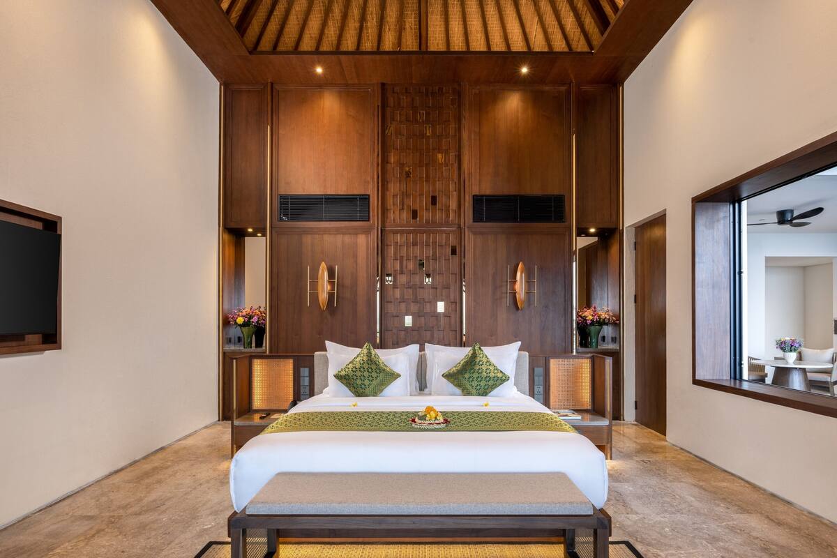 Quarto de hotel moderno com uma cama grande, painéis de madeira e um espelho amplo.