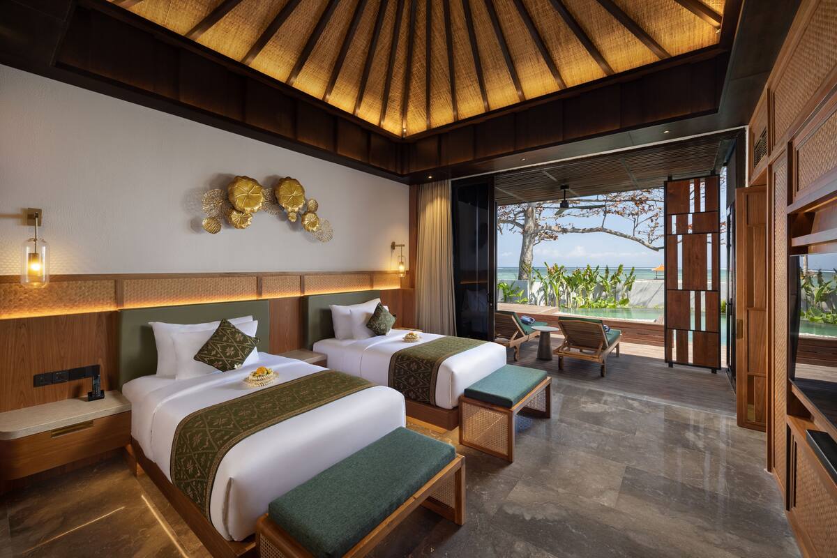 Quarto de hotel moderno com duas camas, área de estar e vista para o mar.