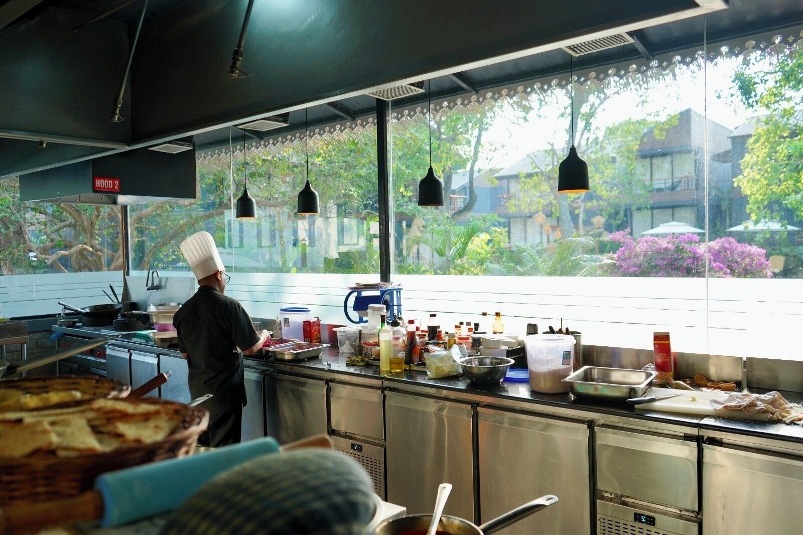 Um chef preparando comida em uma cozinha com grandes janelas e luminárias pendentes.