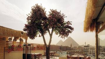 Um lounge no terraço com área de estar acolchoada, mesa e cadeiras, com vista para um horizonte urbano com pirâmides ao fundo.