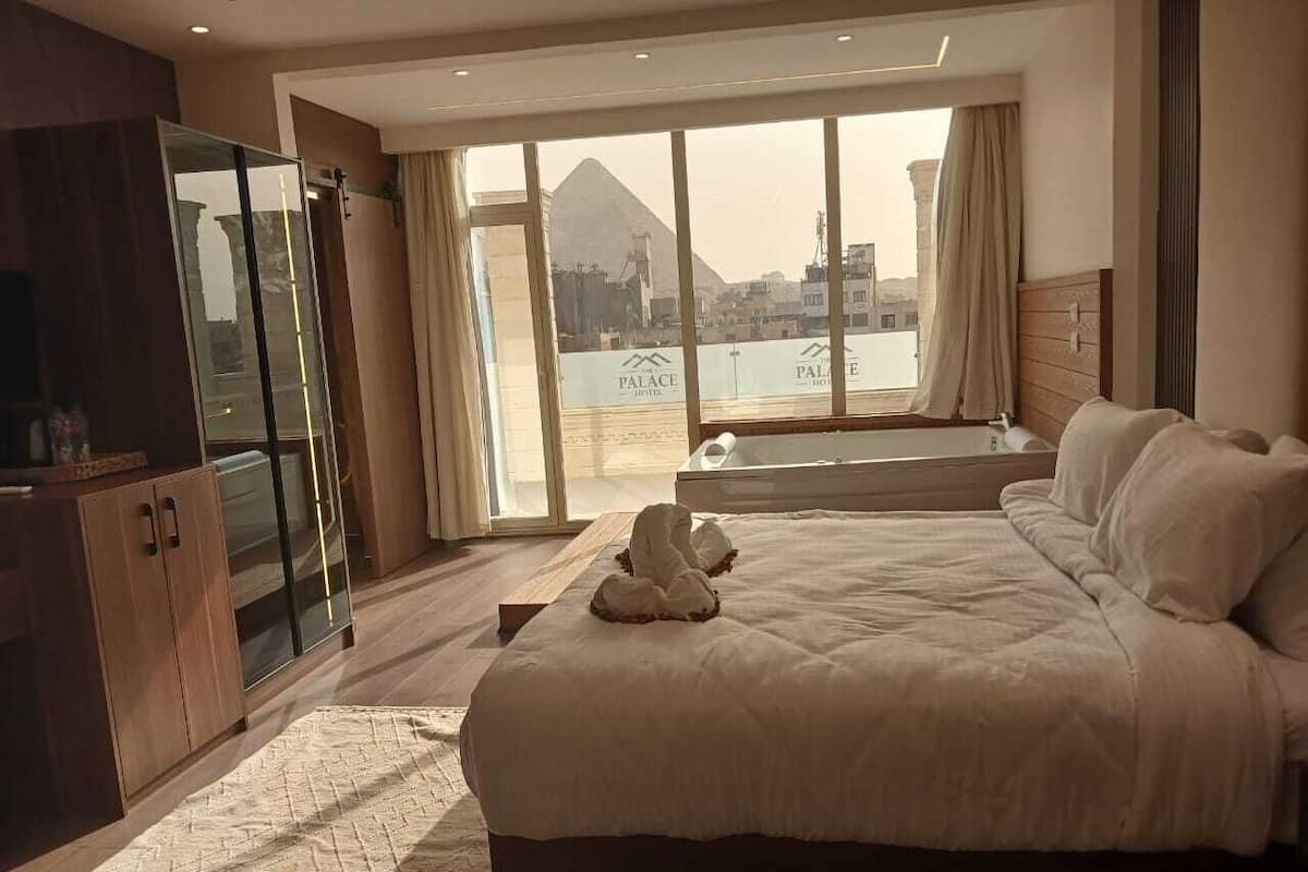 Quarto com uma cama grande, um guarda-roupa de madeira e vista para uma montanha através de grandes janelas.