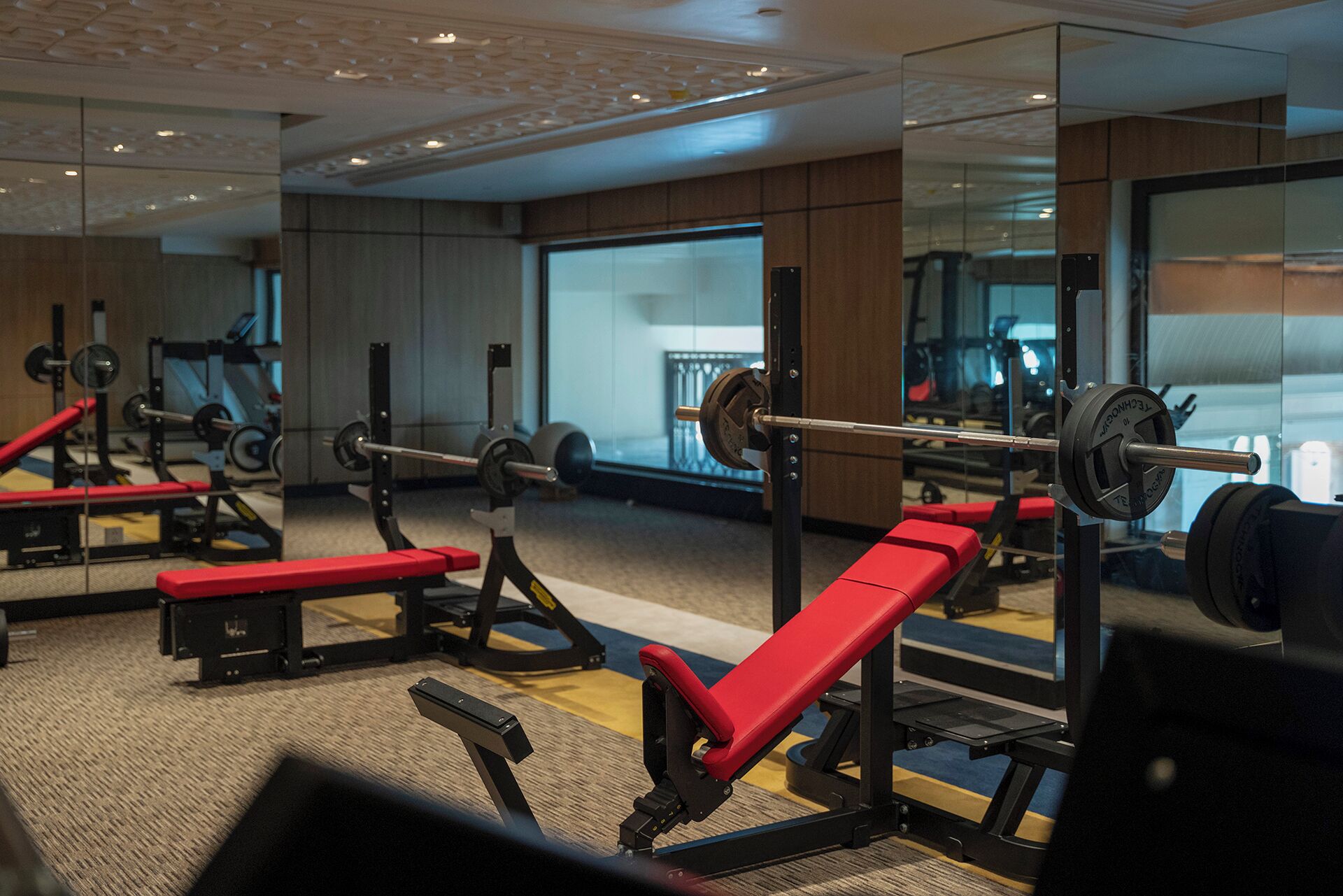 Uma academia com equipamentos de musculação, espelhos e piso coberto por carpete.
