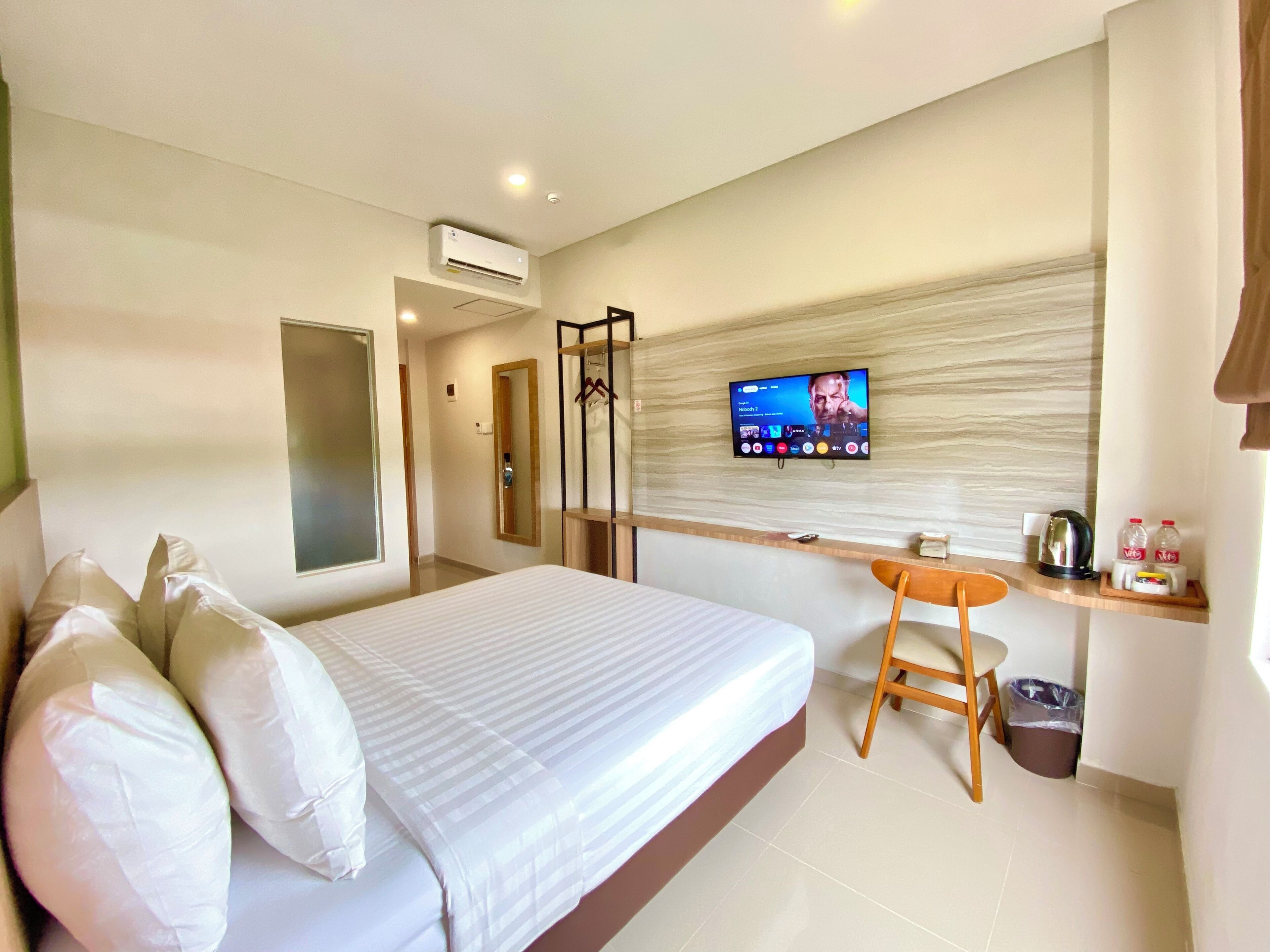 Quarto de hotel com cama, televisão na parede, secretária com cadeira e pequeno espaço com artigos de higiene pessoal.