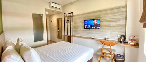 Quarto de hotel com cama, televisão na parede, secretária com cadeira e pequeno espaço com artigos de higiene pessoal.